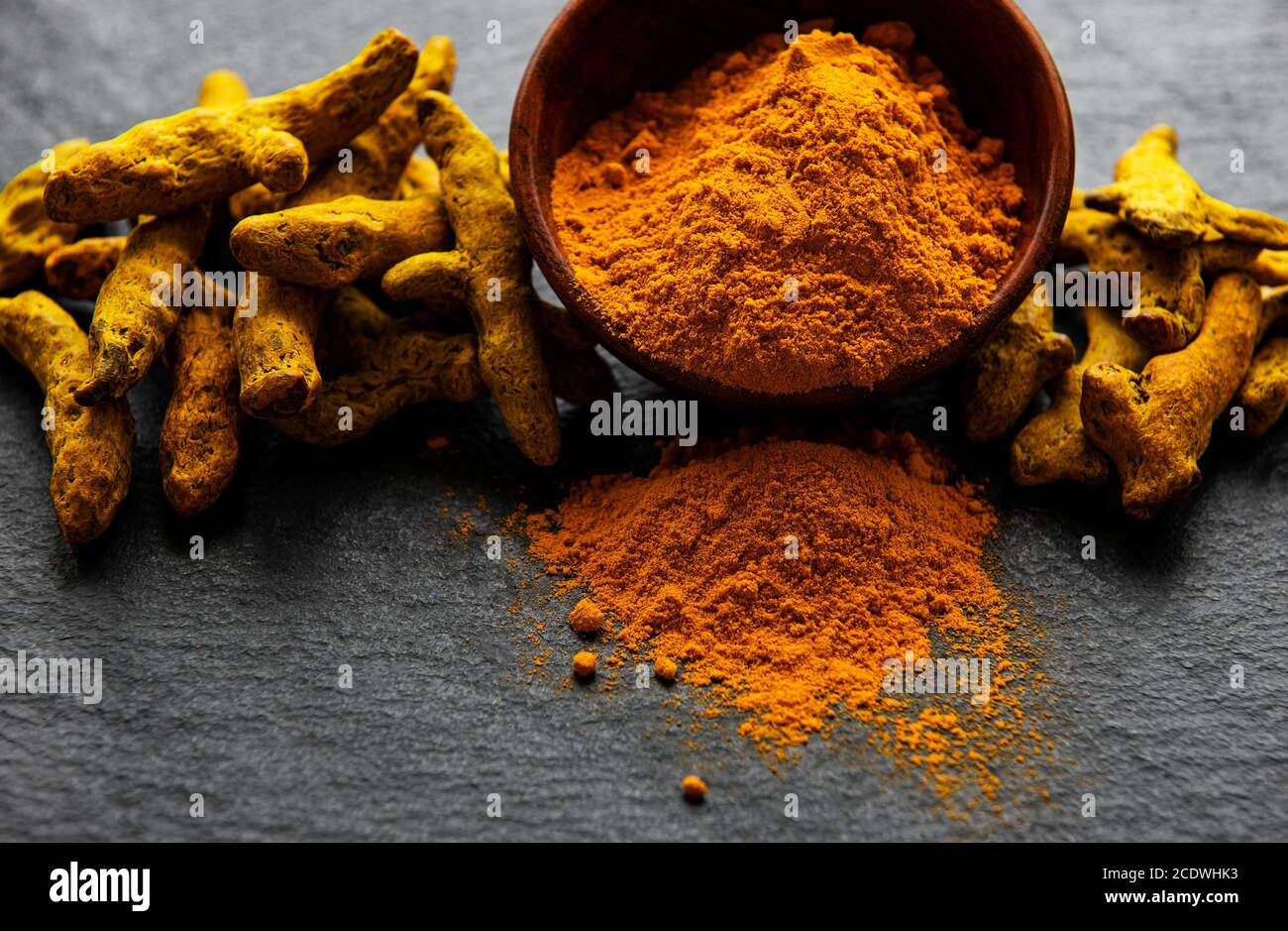 Yellow turmeric powder and dry roots on black stone background Stock ...