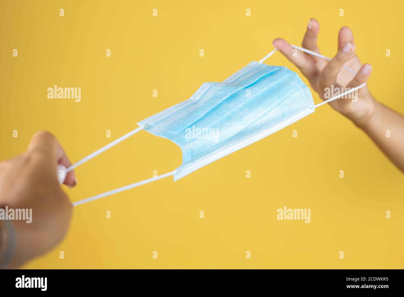 Hand over isolated yellow background holding a mask Stock Photo - Alamy
