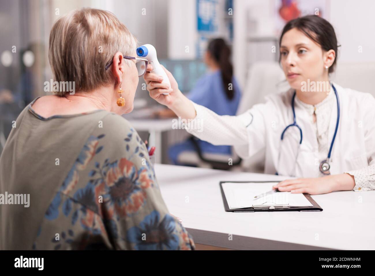 Young doctor using infrared thermometer to take senior woman ...