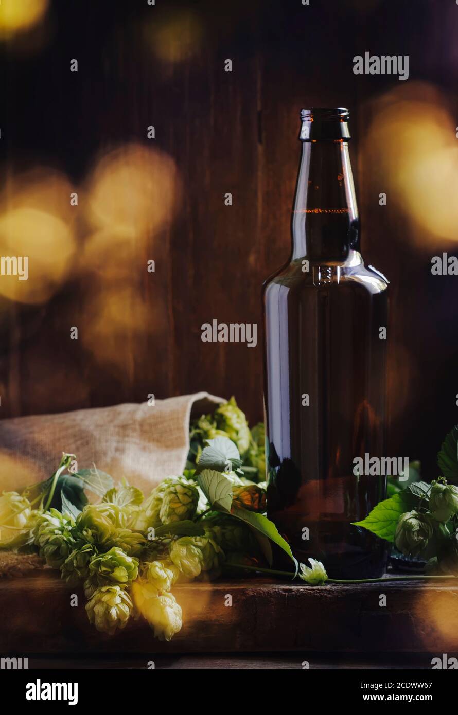 Dark beer bottle, ale or stout iin big glass with hop cones, wooden bar ...