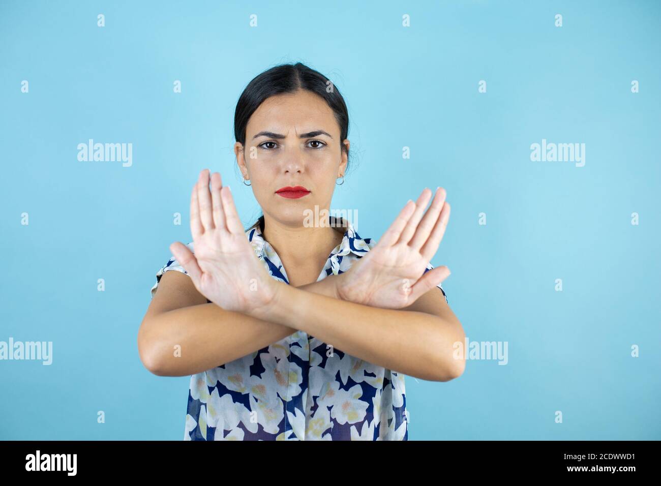 Young beautiful woman over isolated blue background serious and doing ...