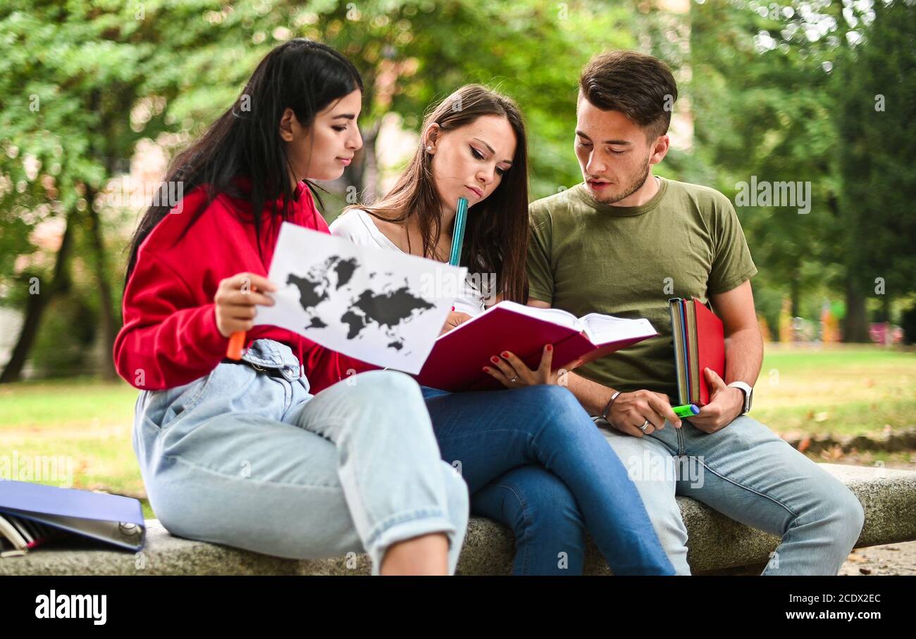 Three students studying together sitting on a bench outdoor Stock Photo ...