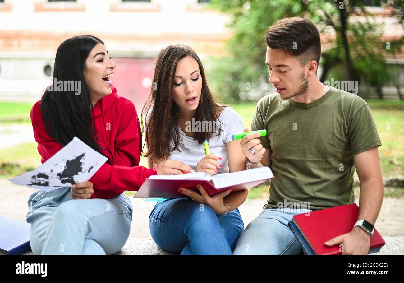 Three students studying together sitting on a bench outdoor Stock Photo ...