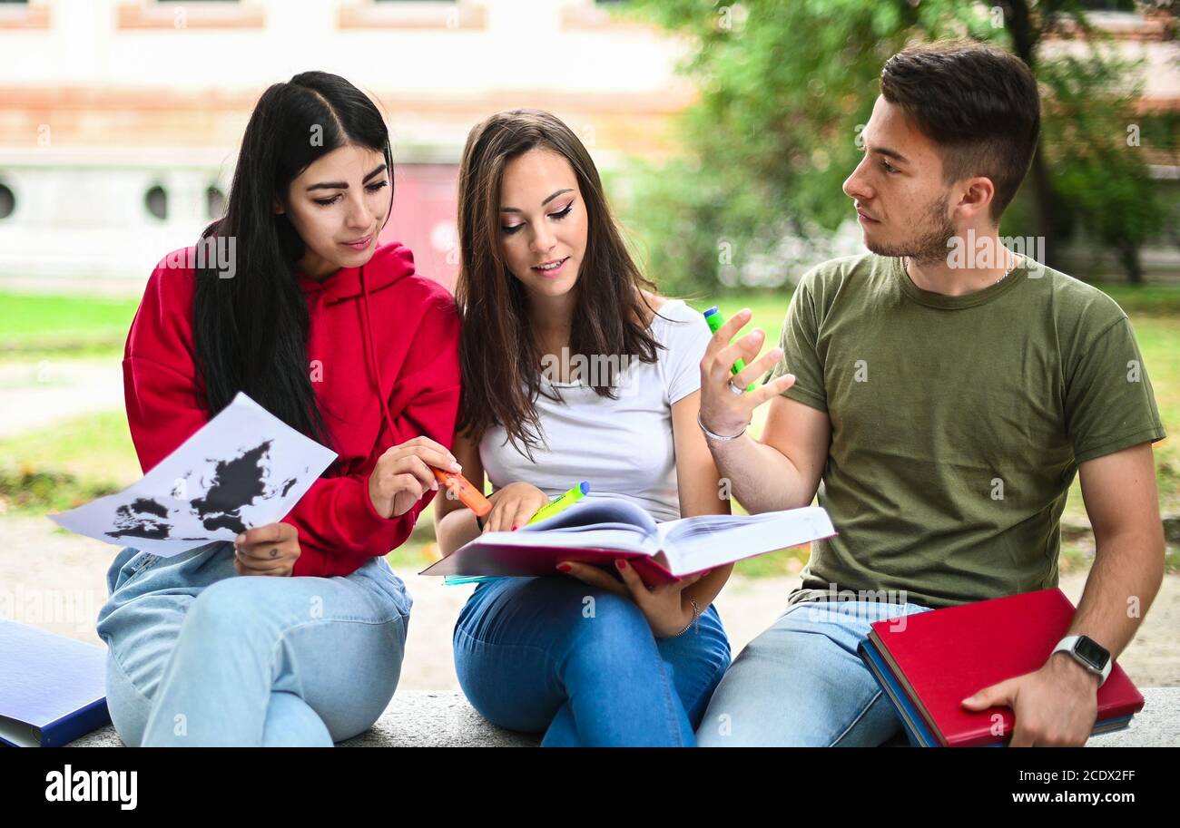 Three students studying together sitting on a bench outdoor Stock Photo ...