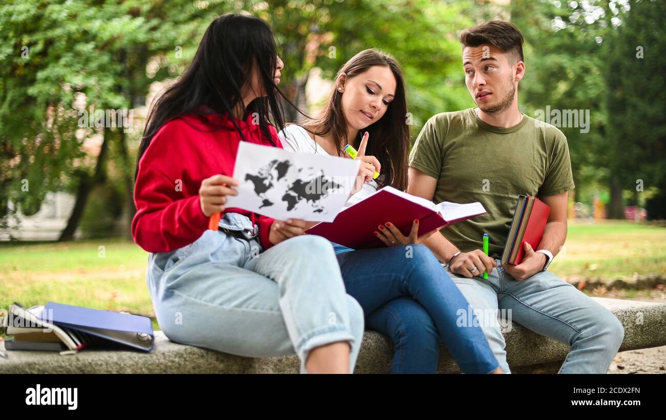 Three students studying together sitting on a bench outdoor Stock Photo ...