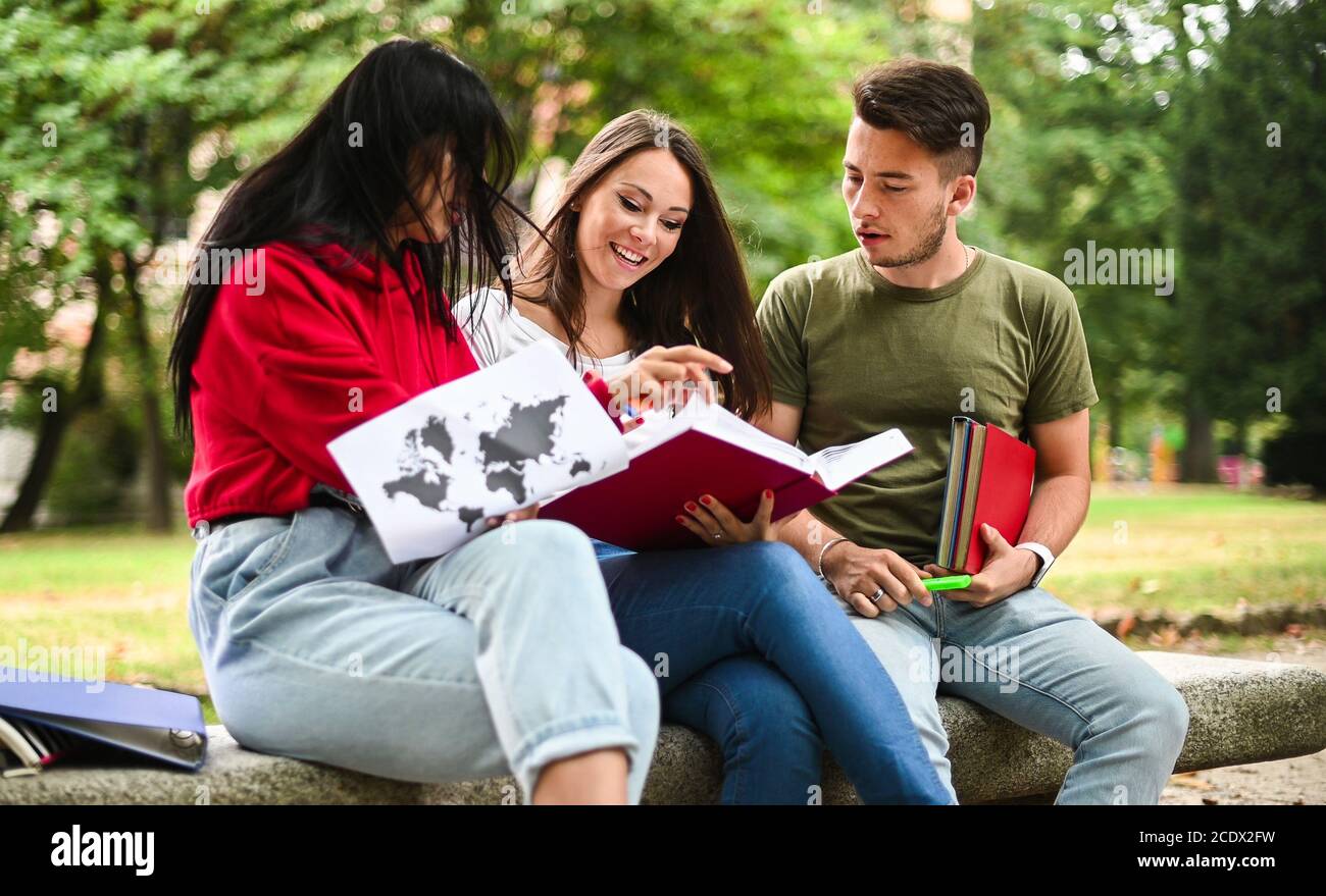 Three students studying together sitting on a bench outdoor Stock Photo ...
