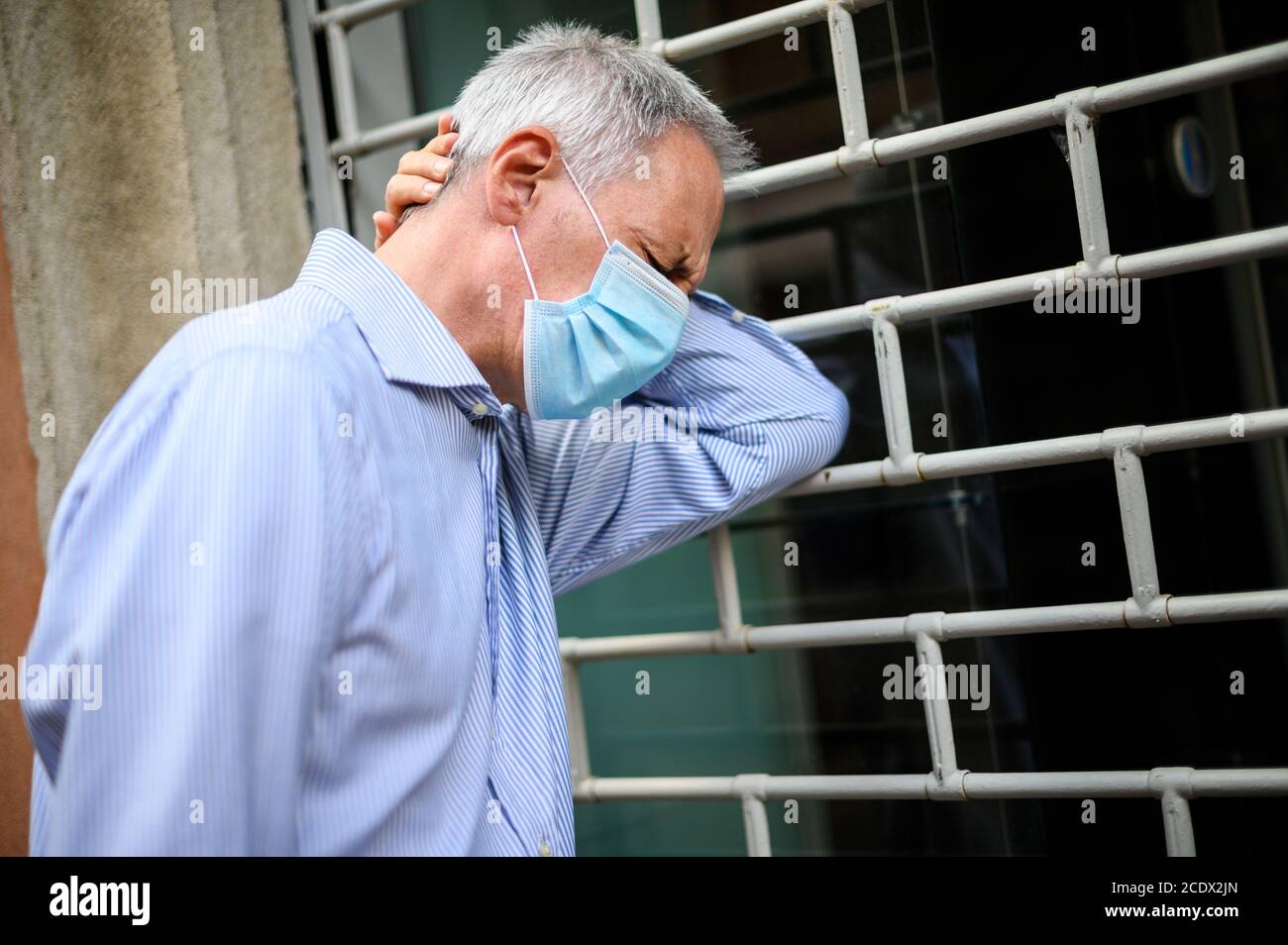 Senior storekeepr wearing a mask and getting sad in front of his closed ...