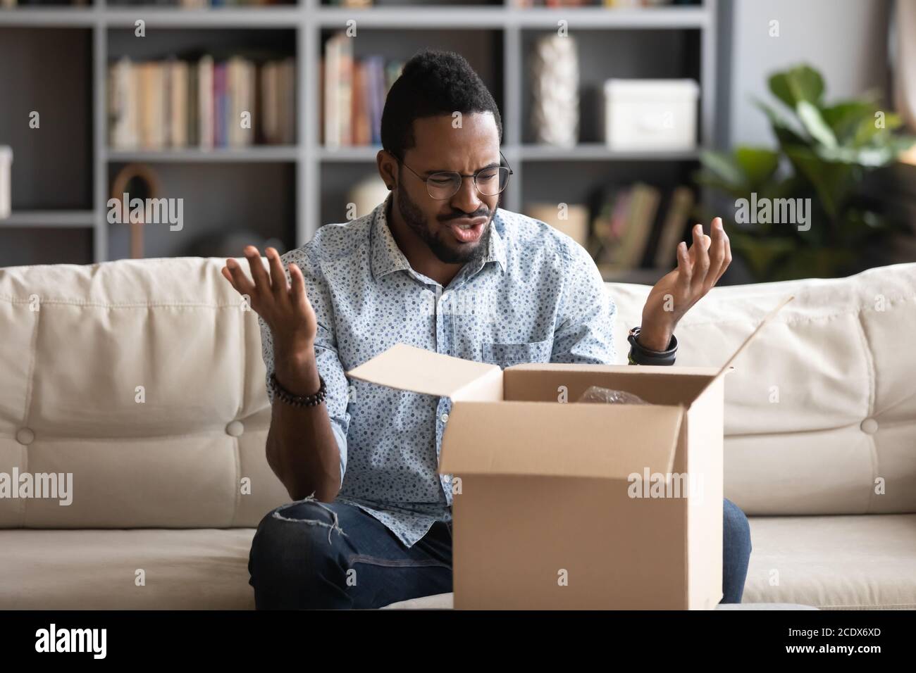 Angry irritated African American man dissatisfied by received parcel ...