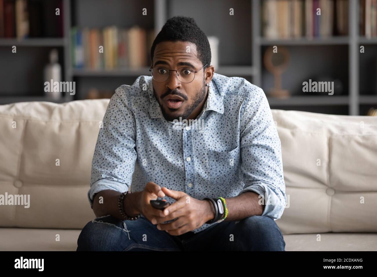 Shocked African American man wearing glasses watching interesting tv ...