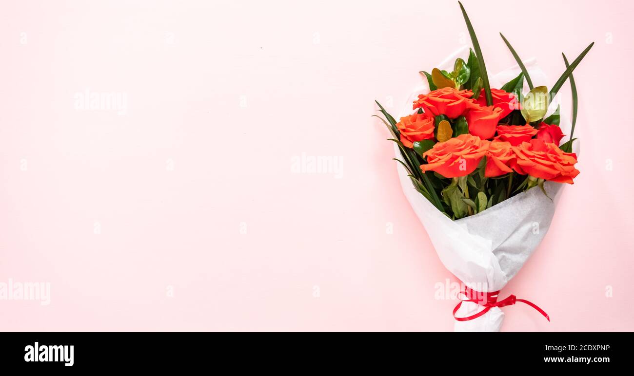 Flat lay. Bouquet of red roses and green leaves on a pink background ...