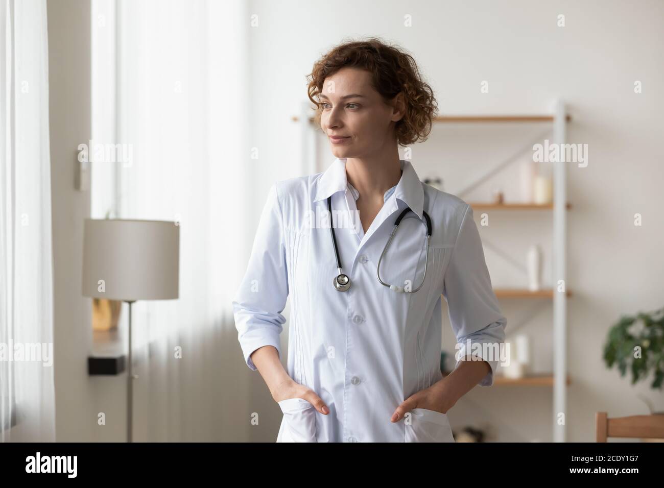 Dreamy young woman doctor wearing uniform looking to aside, visualizing ...