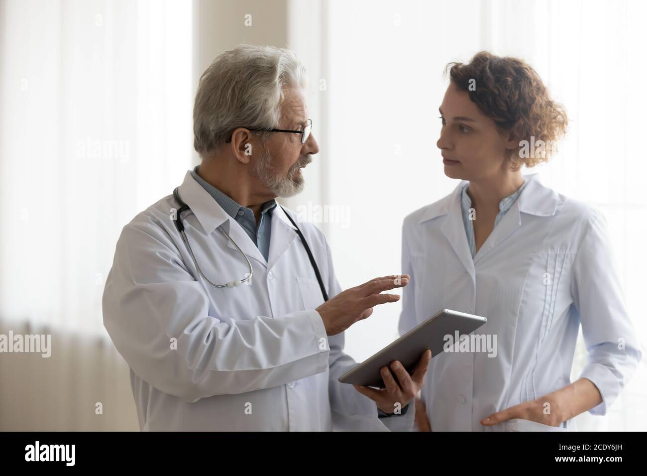 Serious mature doctor and young nurse talking, working together Stock ...