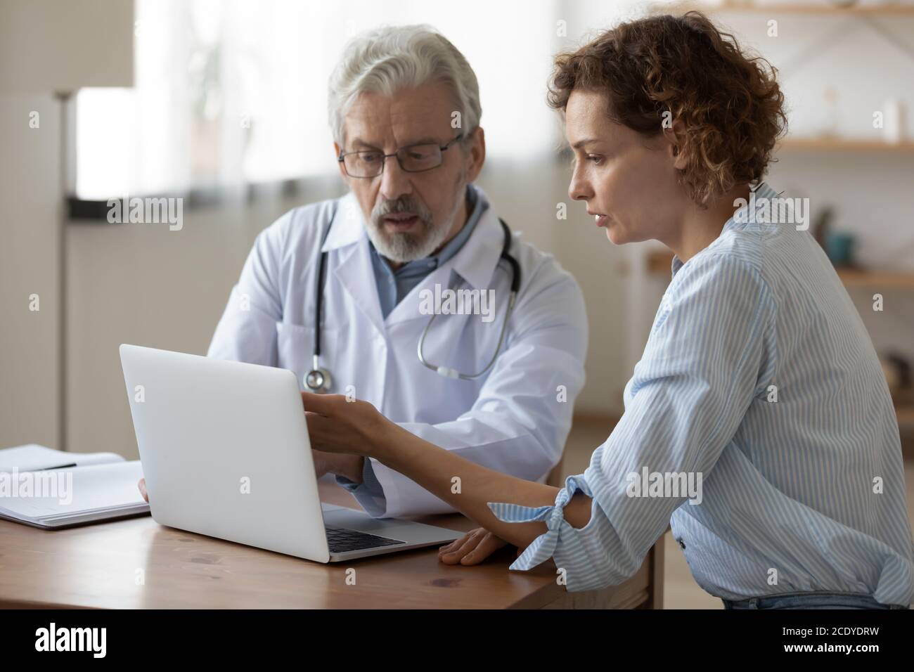 Serious mature doctor showing checkup result on laptop to patient Stock ...