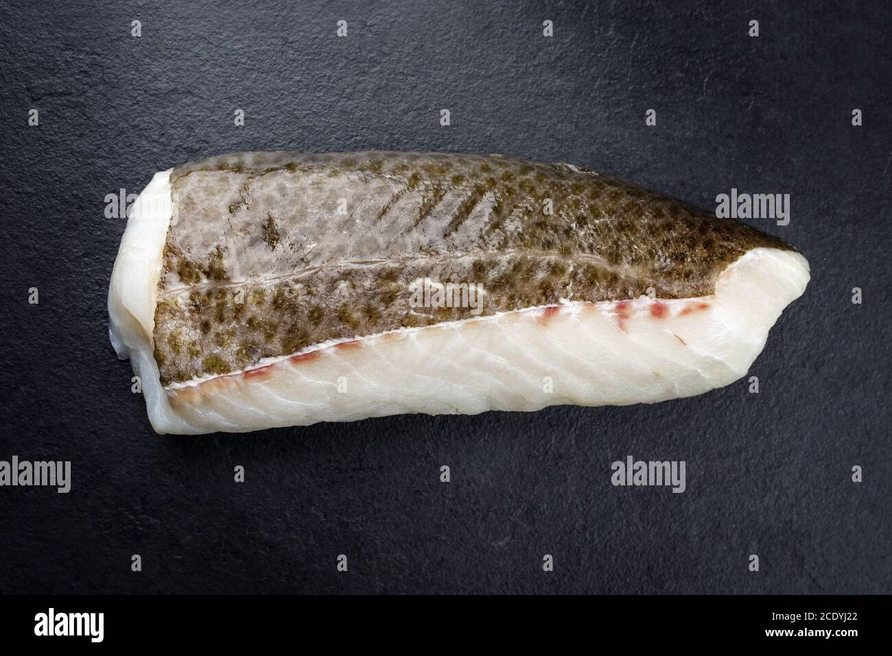 Raw Norwegian skrei cod fish filet with skin as closeup on black board ...