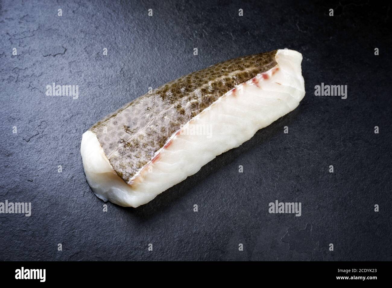 Raw Norwegian skrei cod fish filet with skin as closeup on black board ...