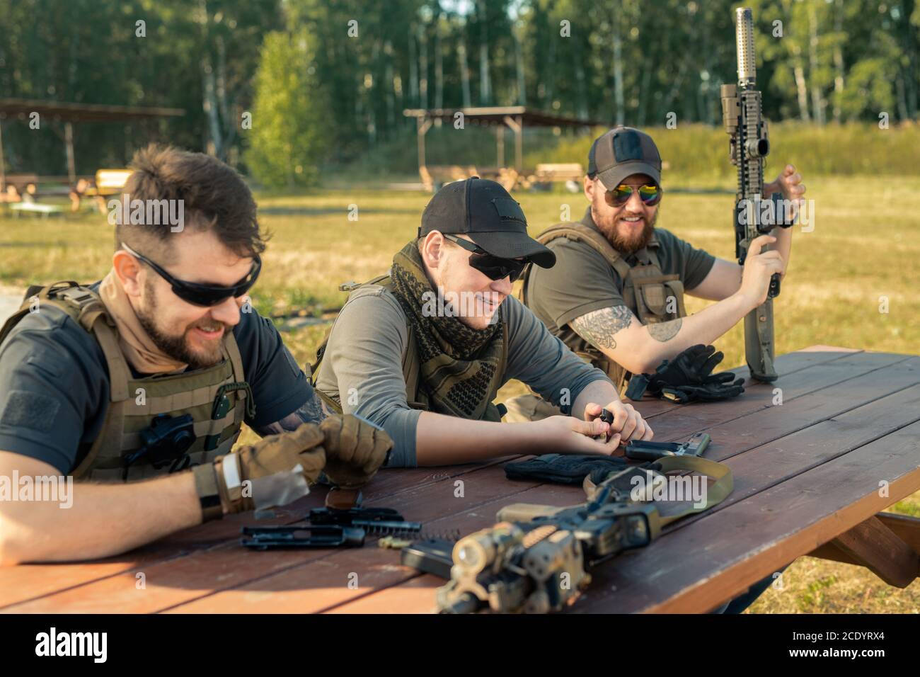 Positive young men in body armors sitting at wooden table and chatting ...