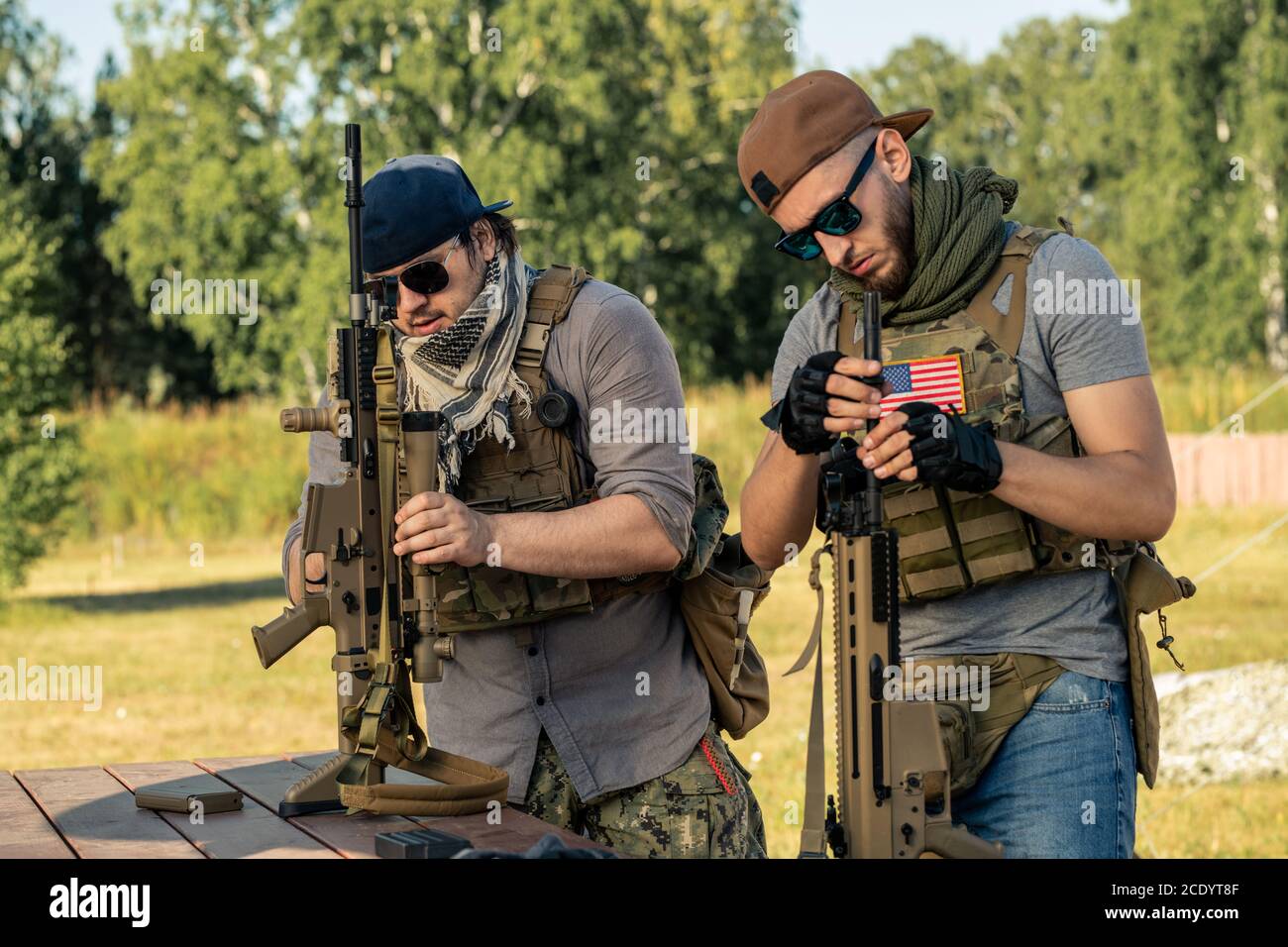 Young American men in vests and caps checking rifles before shooting at ...
