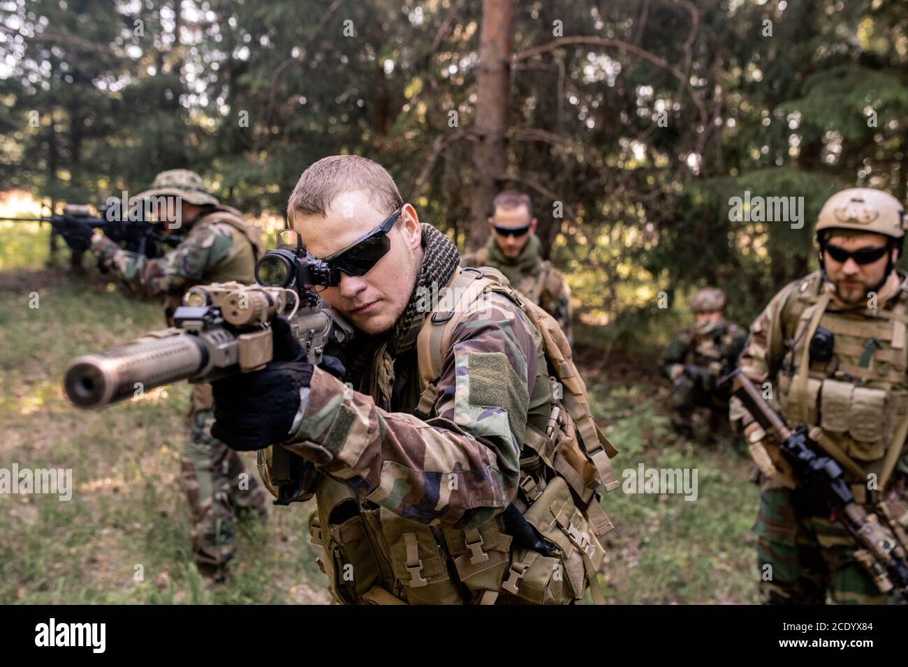Focused armed soldiers in uniform carrying rifles and examining forest ...
