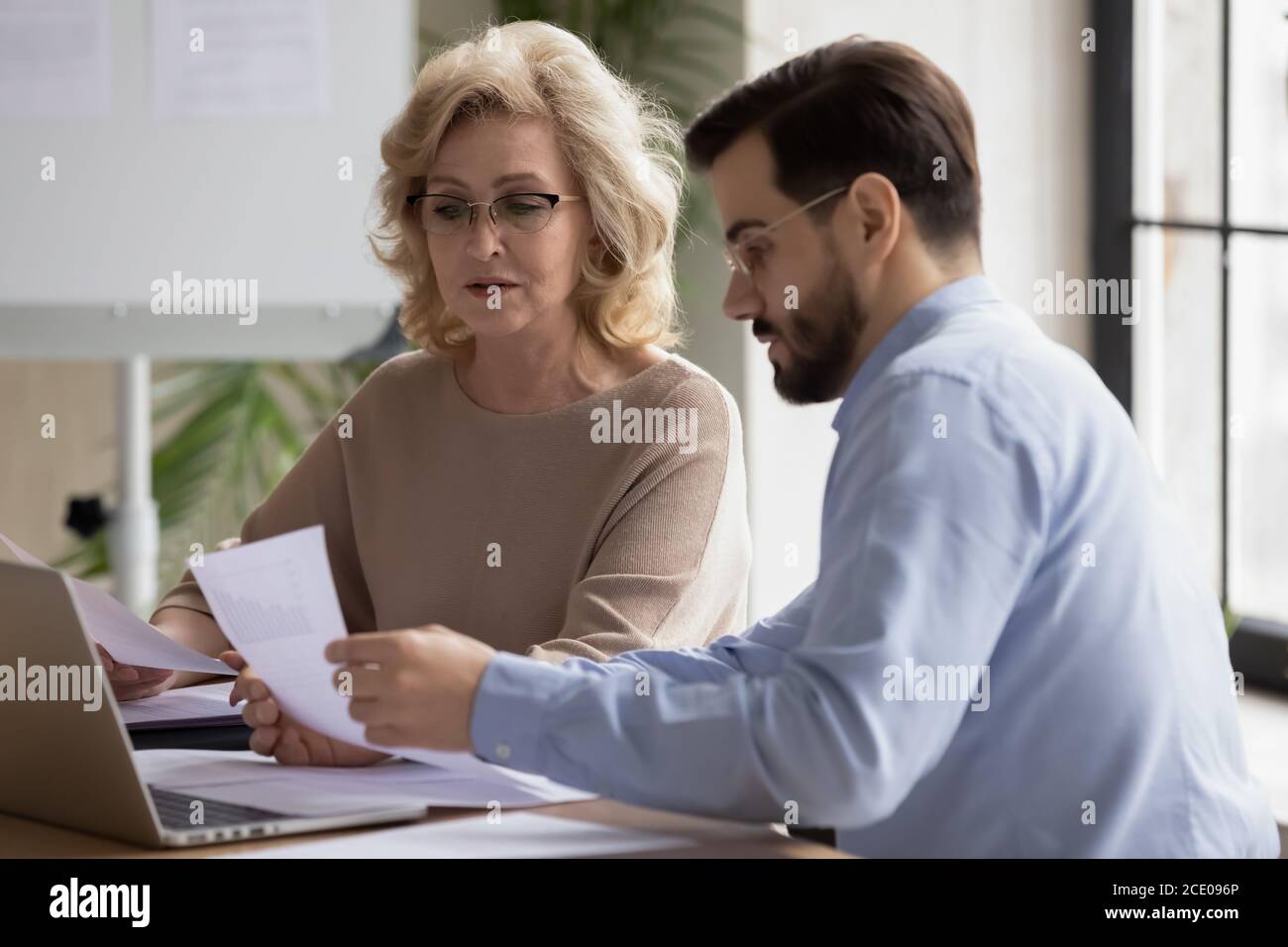 Focused middle aged 50s businesswoman discussing reports with employee ...