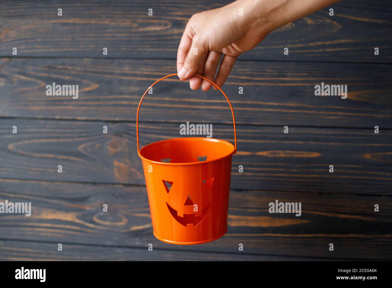Hand holding orange trick or treat bucket for candy on black wooden ...