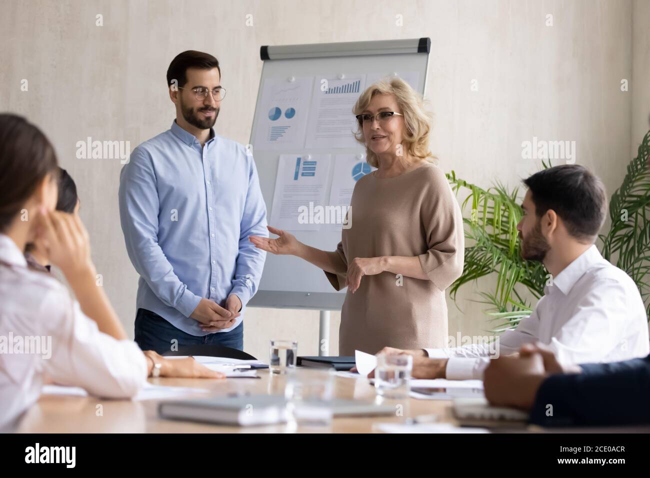 Smiling middle aged mature leader introducing new worker to colleagues ...
