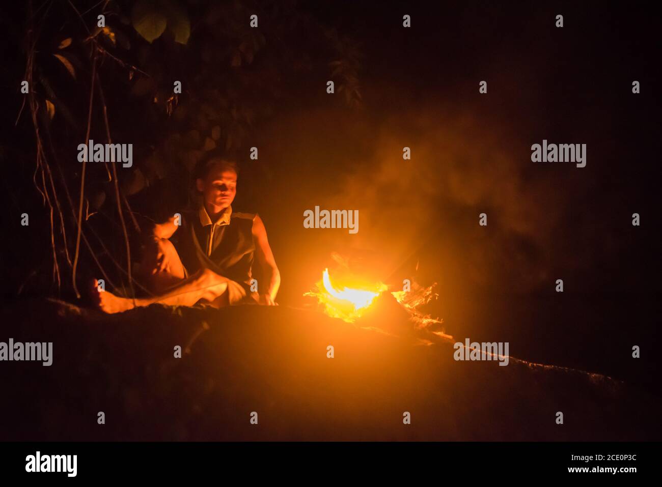 The guide on the rock is watching bonfire in the nightly jungle of ...