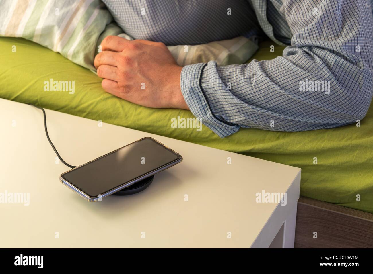 A charging phone on the bedside table next to the bed and a sleeping ...