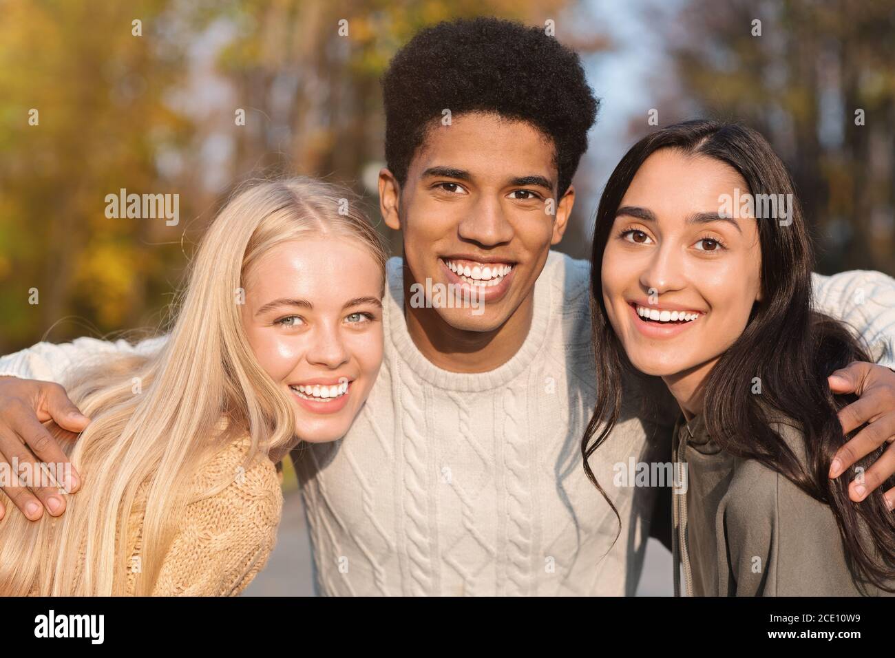 Portrait of three multiethnic friends smiling over park background ...
