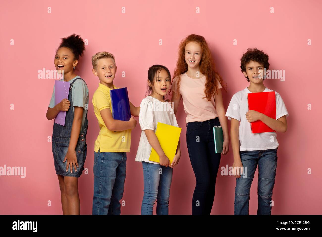 Schooling is fun. Excited diverse pupils holding notebooks over pink ...