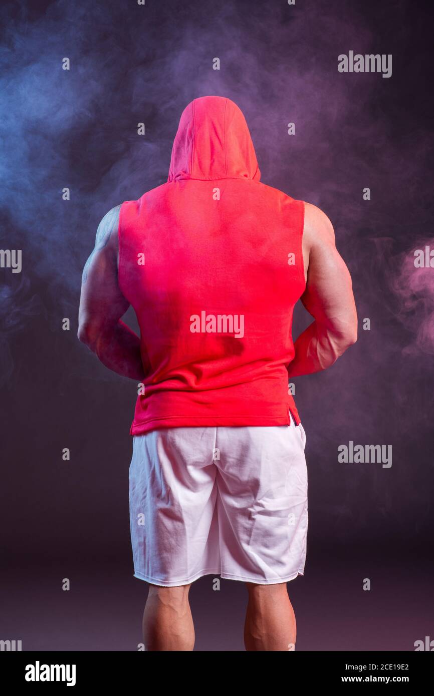 Powerful muscular man with a hood posing in the red sweatshirt. Back ...