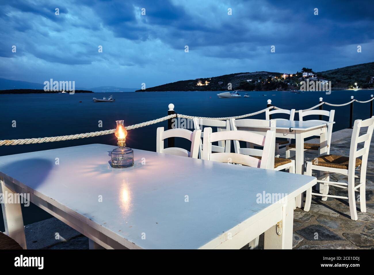 Traditional white wooden tables and chairs of a greek tavern at night ...