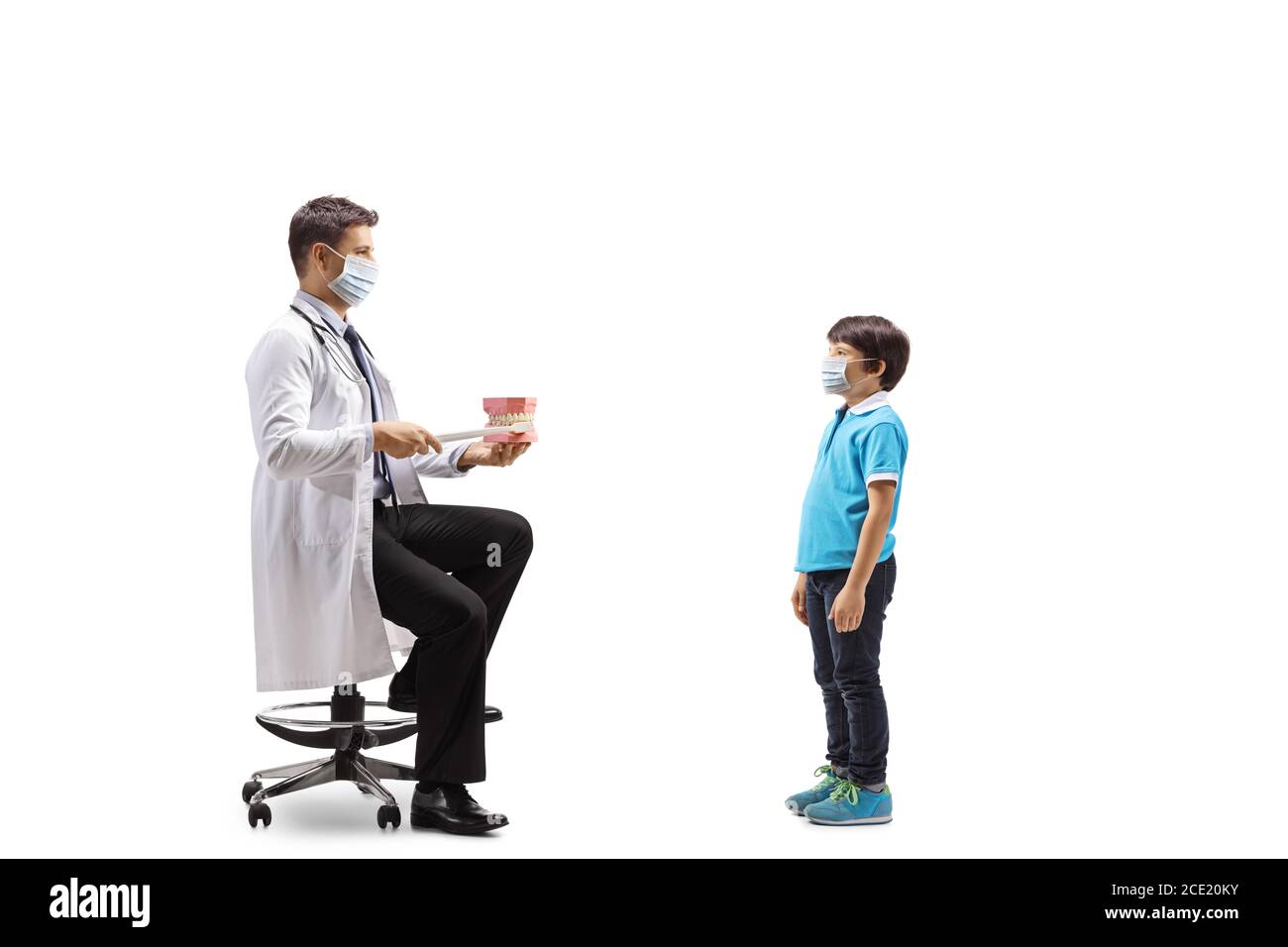 Dentist demonstrating brushing teeth to a schoolboy with a protective ...