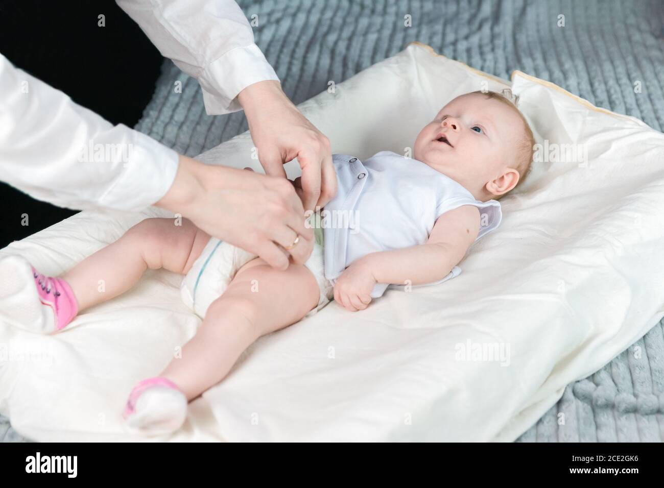 Mom changes the babys diaper. The baby is lying on the changing table ...