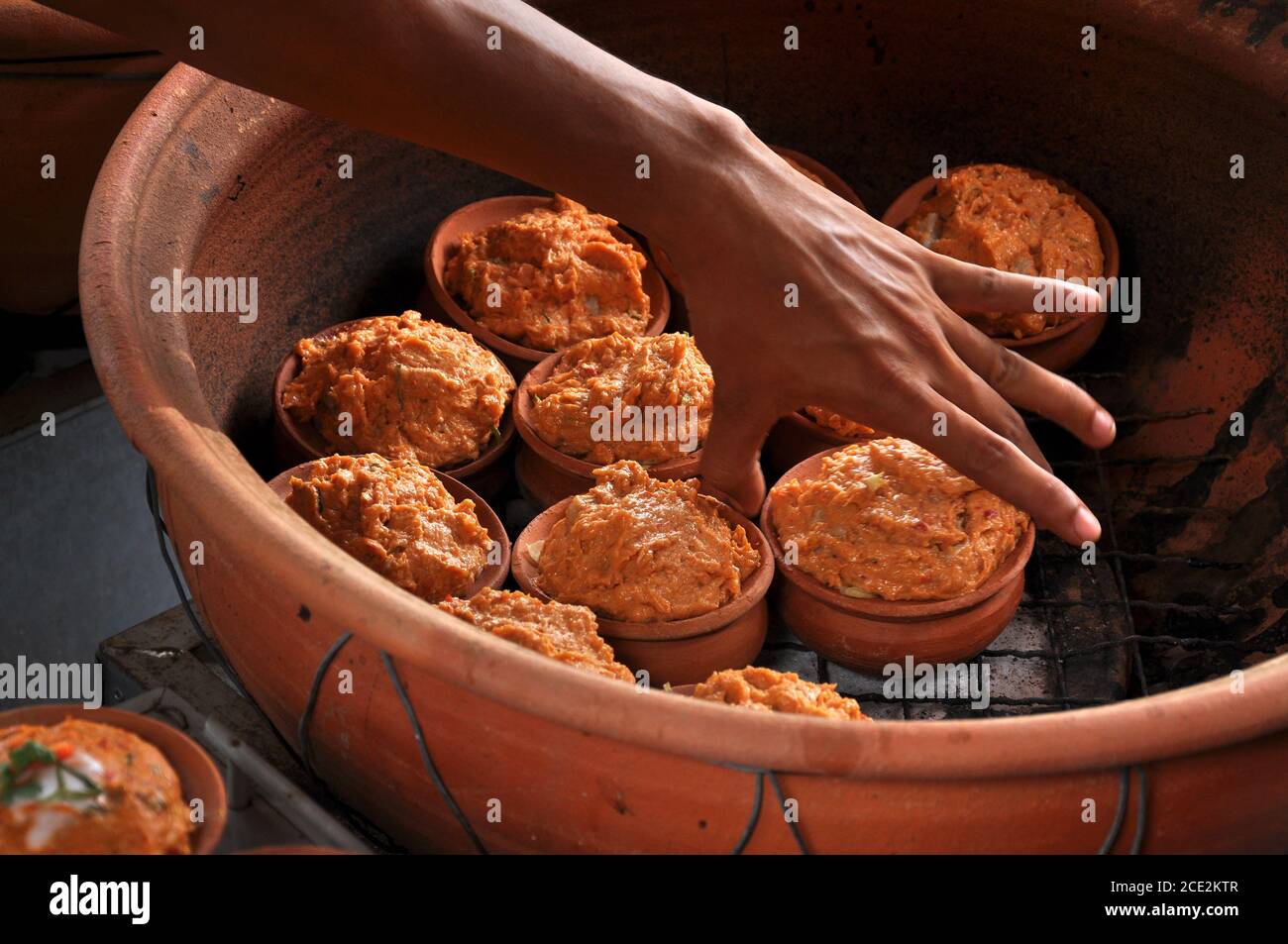 Close up of an ethnic hand reaching into a big clay firing pot filled ...