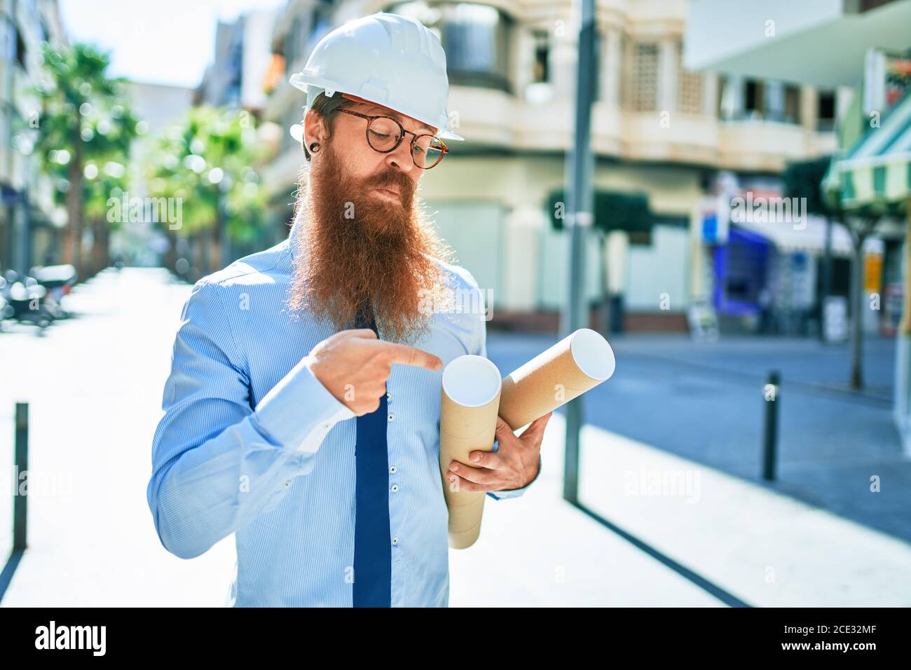 Young redhead architect man with long beard wearing hardhat smiling ...