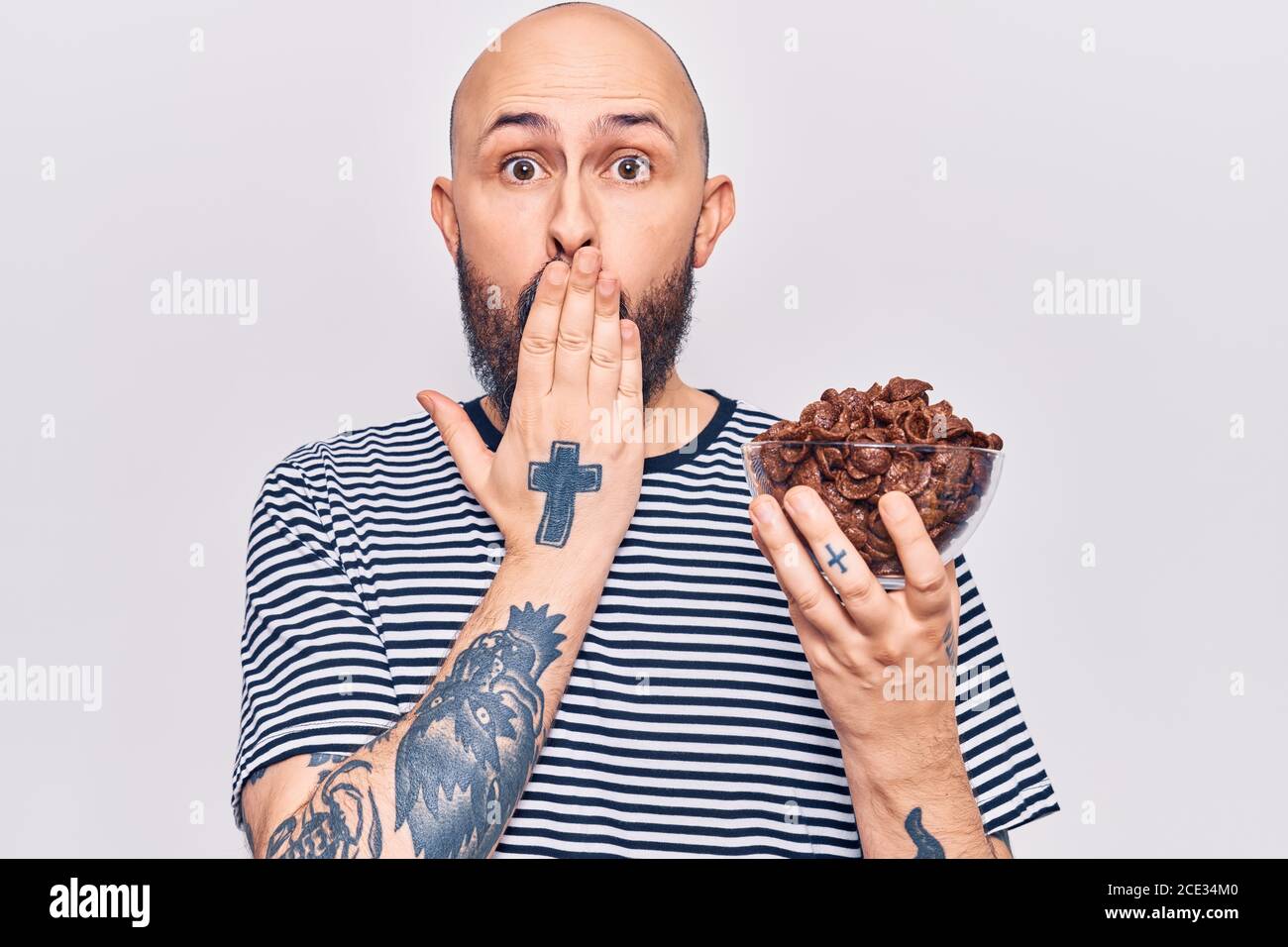 Young handsome man holding chocolate cereals covering mouth with hand ...