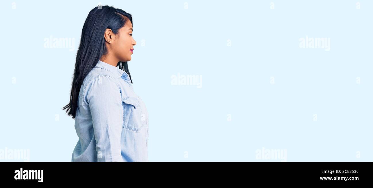 Hispanic woman with long hair wearing casual denim jacket looking to ...