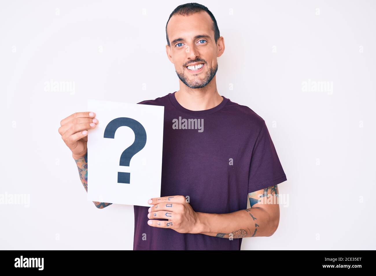 Young handsome man with tattoo holding question mark looking positive ...