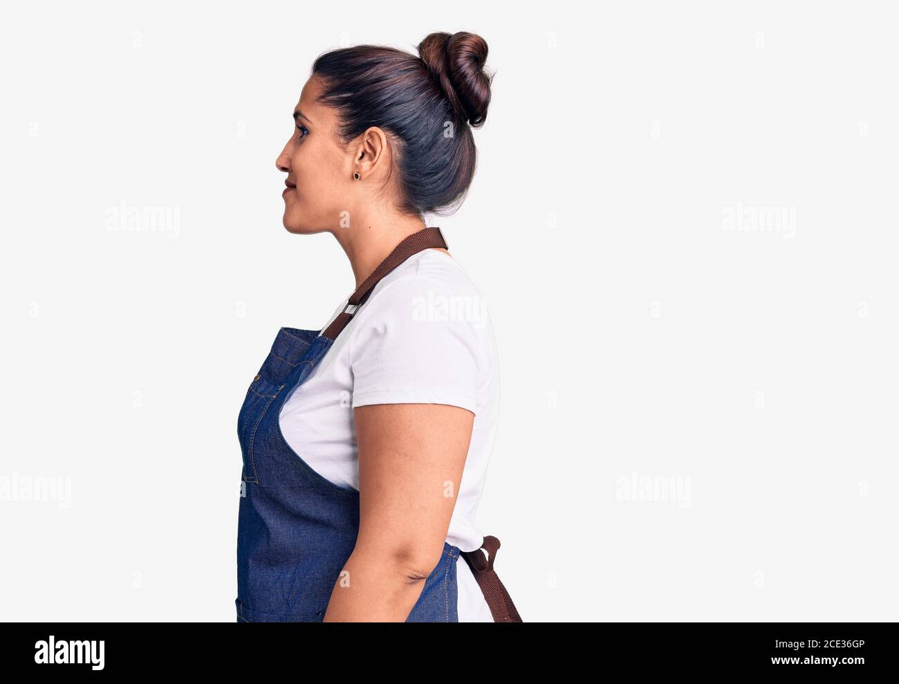 Young beautiful brunette woman wearing apron looking to side, relax ...