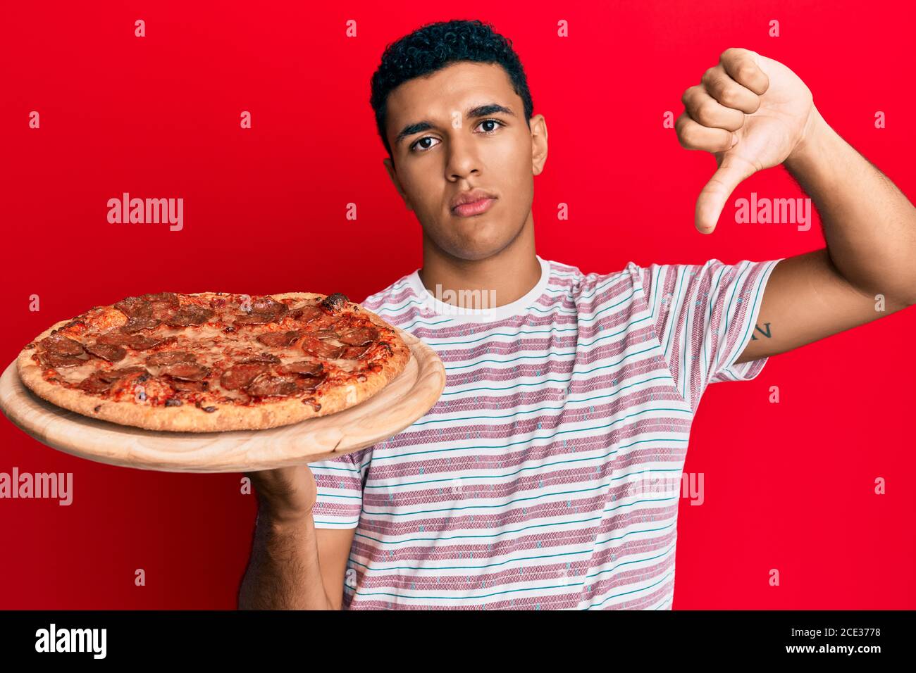 Young arab man holding italian pizza with angry face, negative sign ...