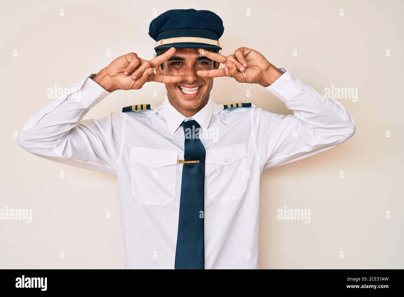 Young hispanic man wearing airplane pilot uniform doing peace symbol ...