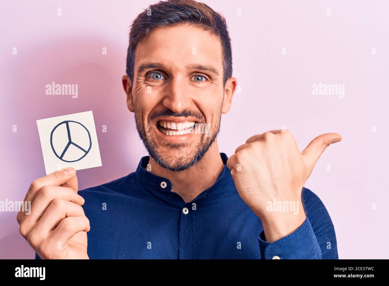 Young handsome man holding reminder with peace symbol over isolated ...