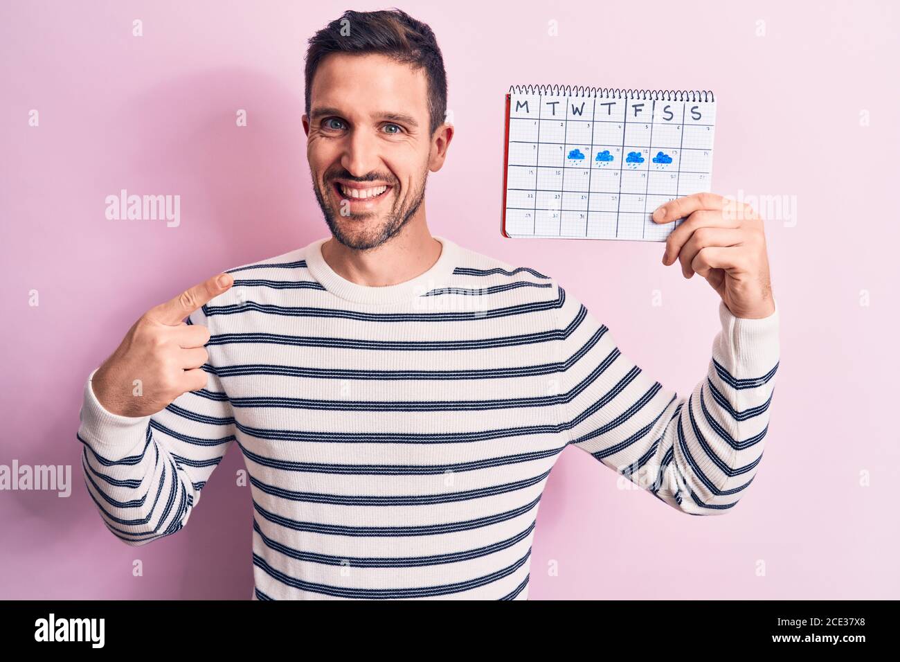Young handsome man holding weather calendar showing rainy week over ...