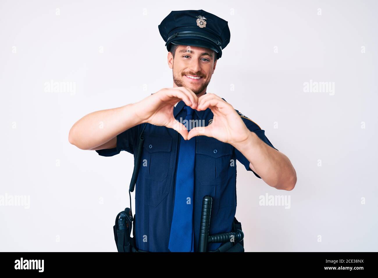 Young caucasian man wearing police uniform smiling in love doing heart ...