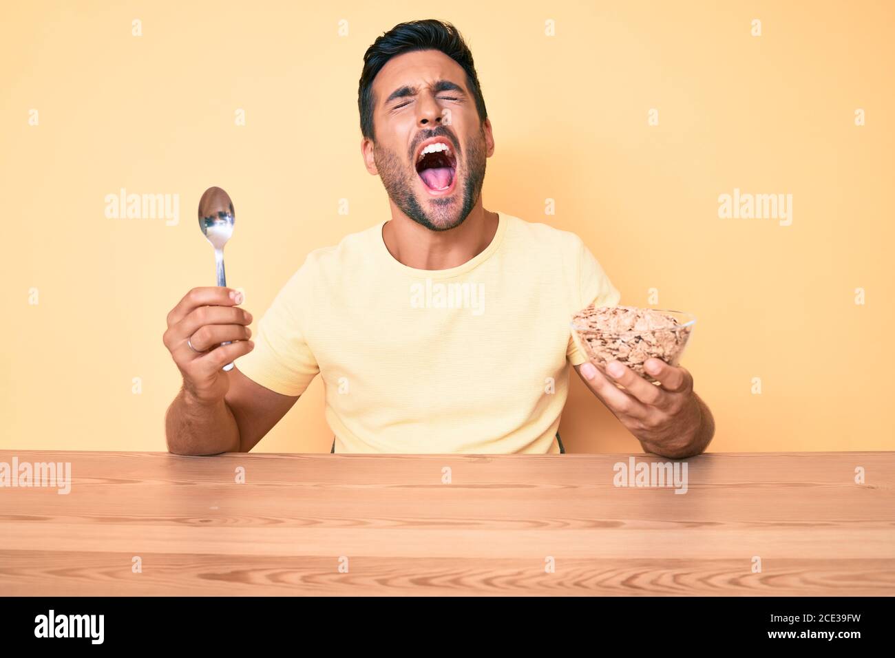 Young handsome hispanic man eating healthy whole grain celears sitting ...