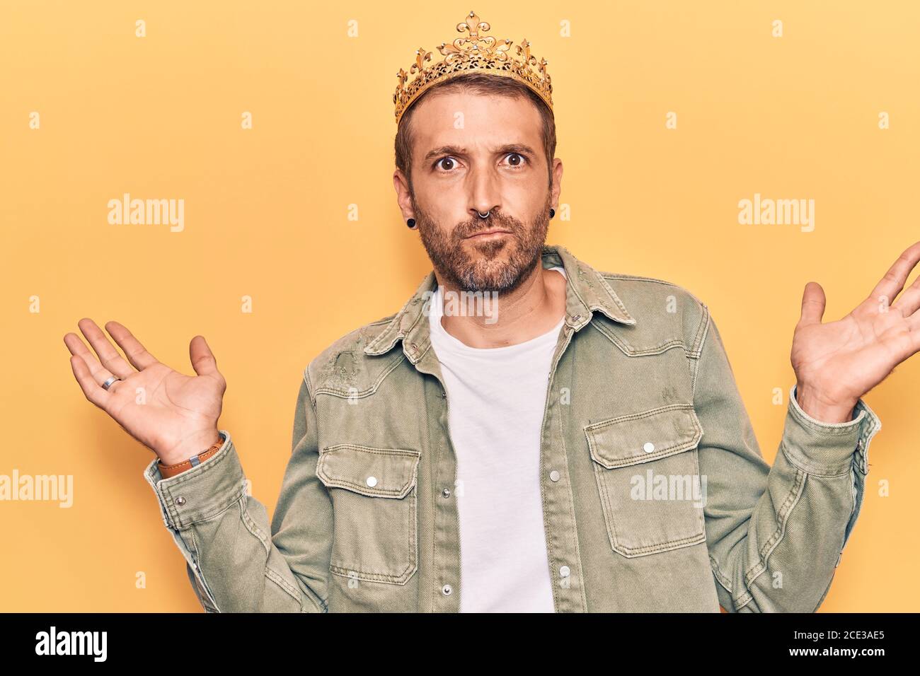 Young handsome man wearing king crown clueless and confused with open ...