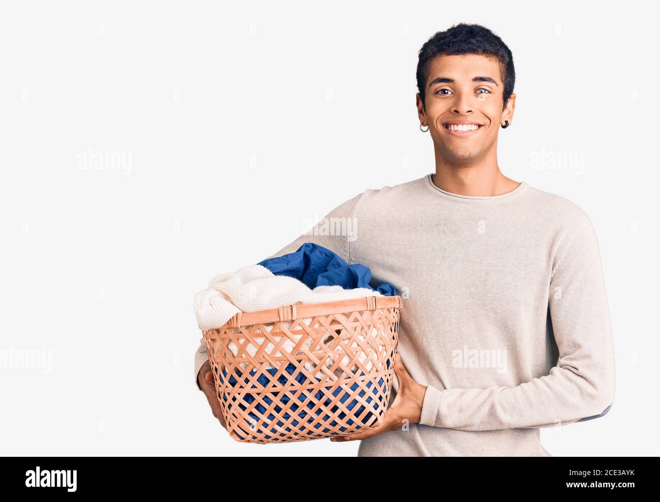Young african amercian man holding laundry basket looking positive and ...