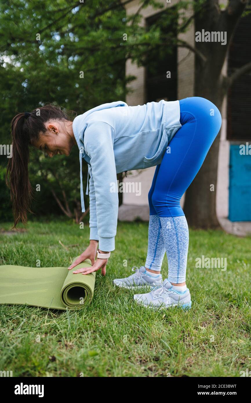 Woman folding roll fitness or yoga mat after working out in the park ...
