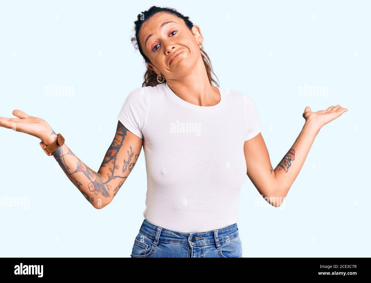 Young hispanic woman with tattoo wearing casual white tshirt clueless ...