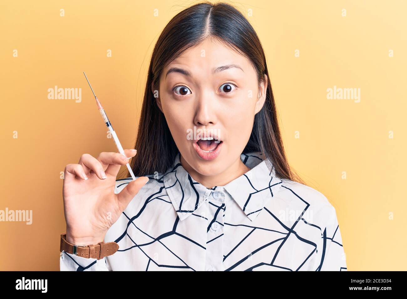 Young beautiful chinese woman holding syringe scared and amazed with ...
